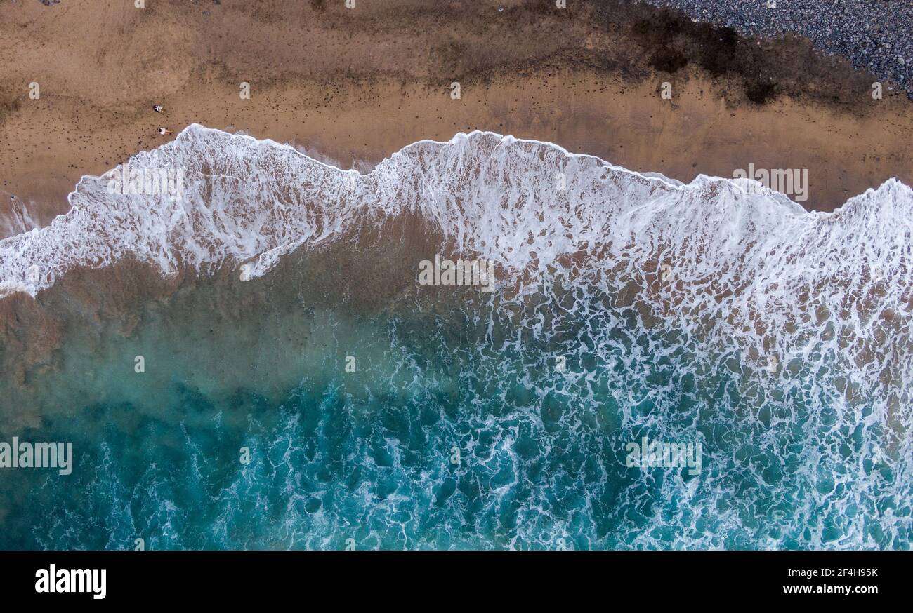 overhead shot of a couple on a beach walking on the shore with wave ...