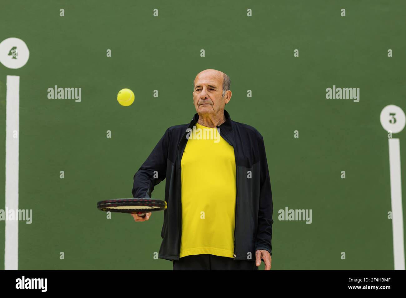 Senior sportsman bouncing ball on racket while preparing for tennis ...