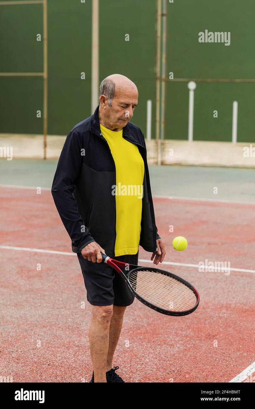 Senior sportsman bouncing ball on racket while preparing for tennis ...