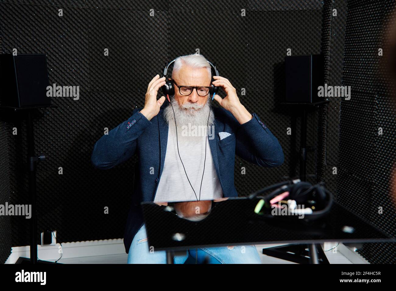 Elderly bearded male in headphones sitting in soundproof room during ...
