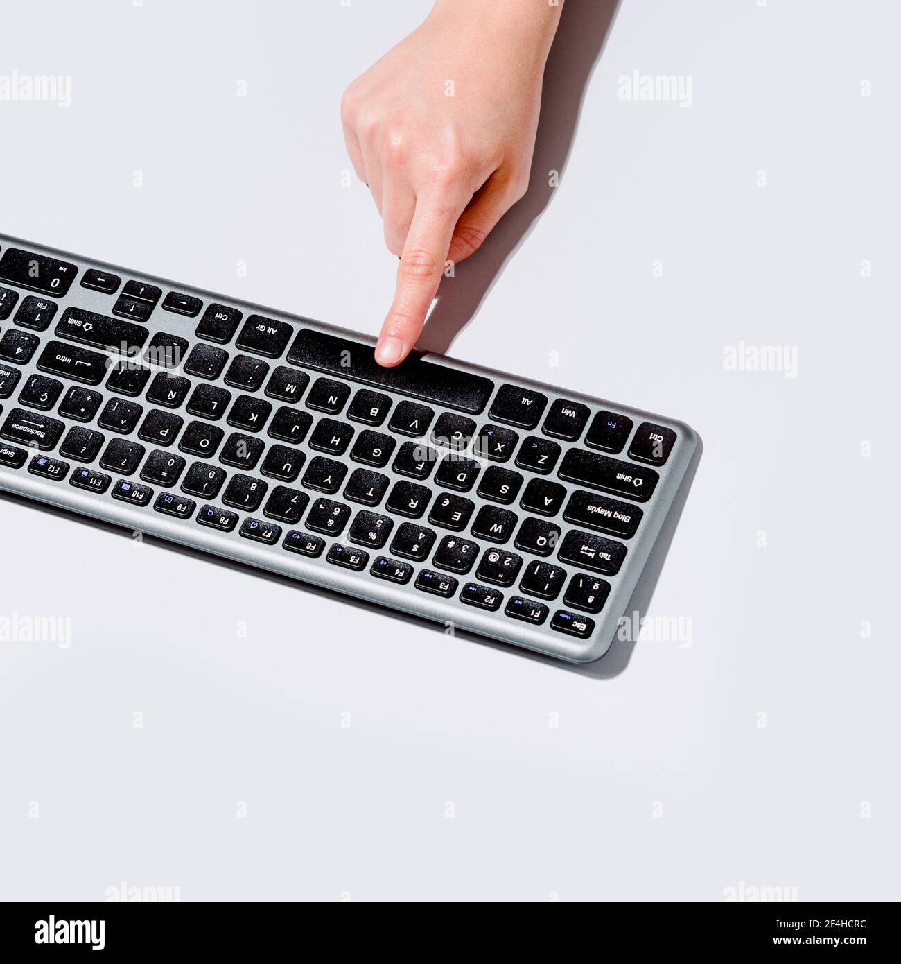 From above anonymous person pushing button on computer keyboard on gray ...