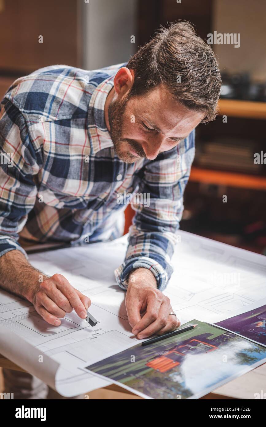 Delighted male architect standing at table and drawing plan of house on ...