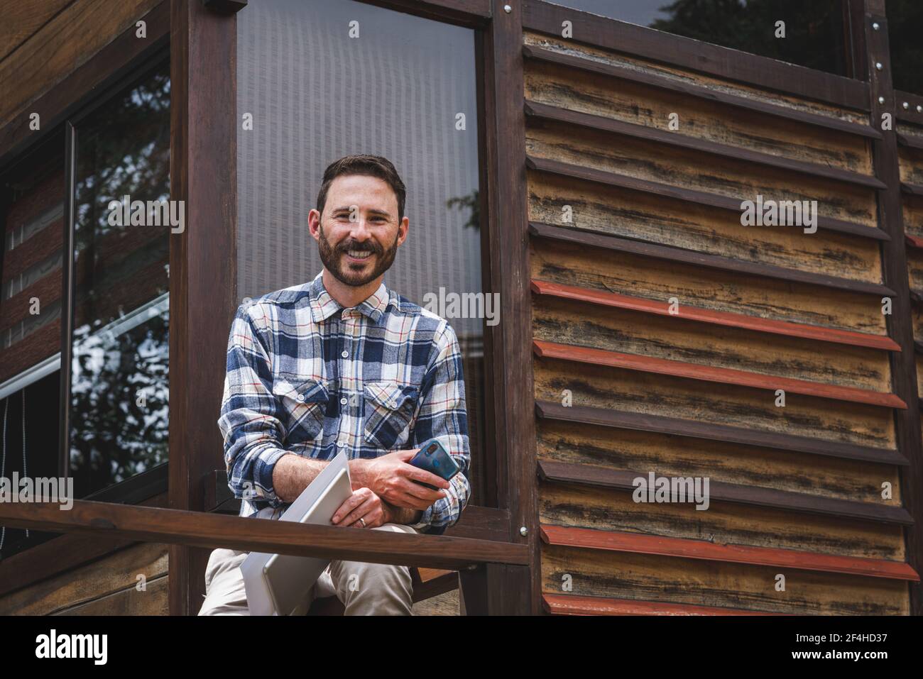 Low angle of smiling male architect with paper drafts and devices ...