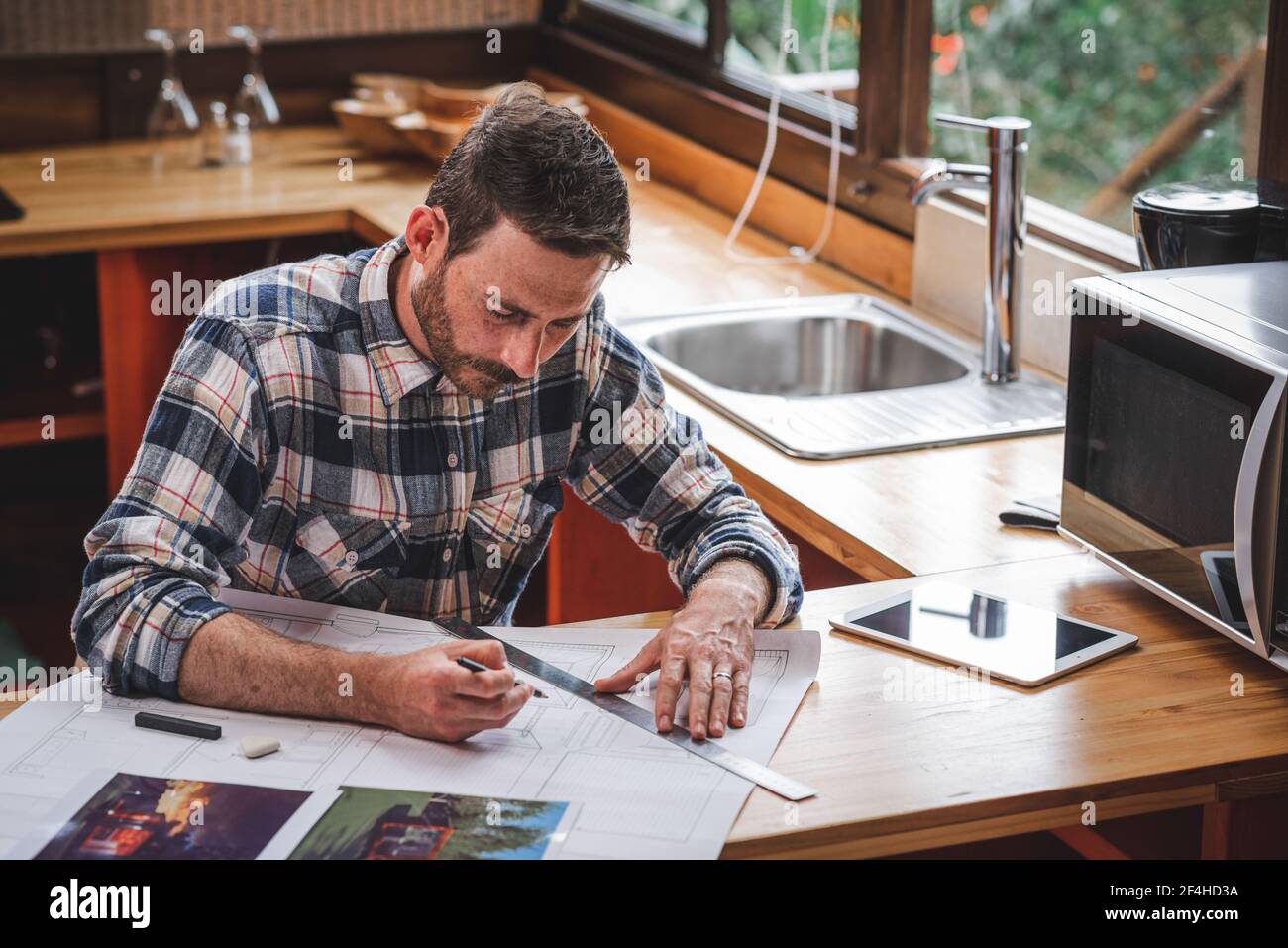Serious male architect sitting at table in kitchen and drawing ...