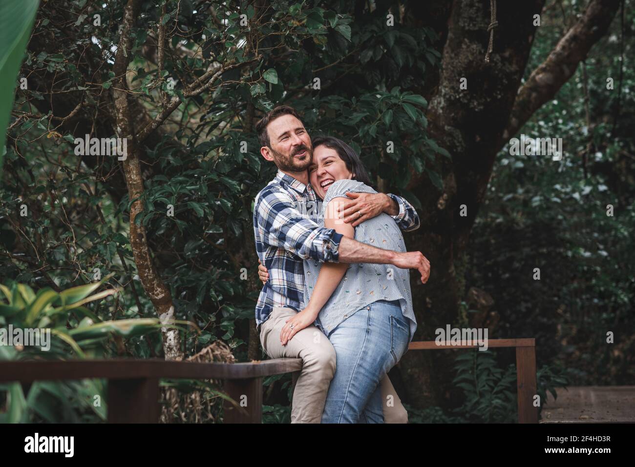 Cheerful couple in love embracing on wooden terrace of house in woods ...