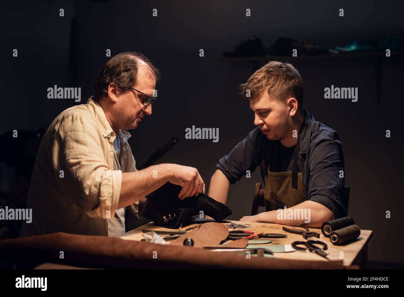 a respectable elderly shoemaker conducts a master class for a young boy on making shoes by hand ...