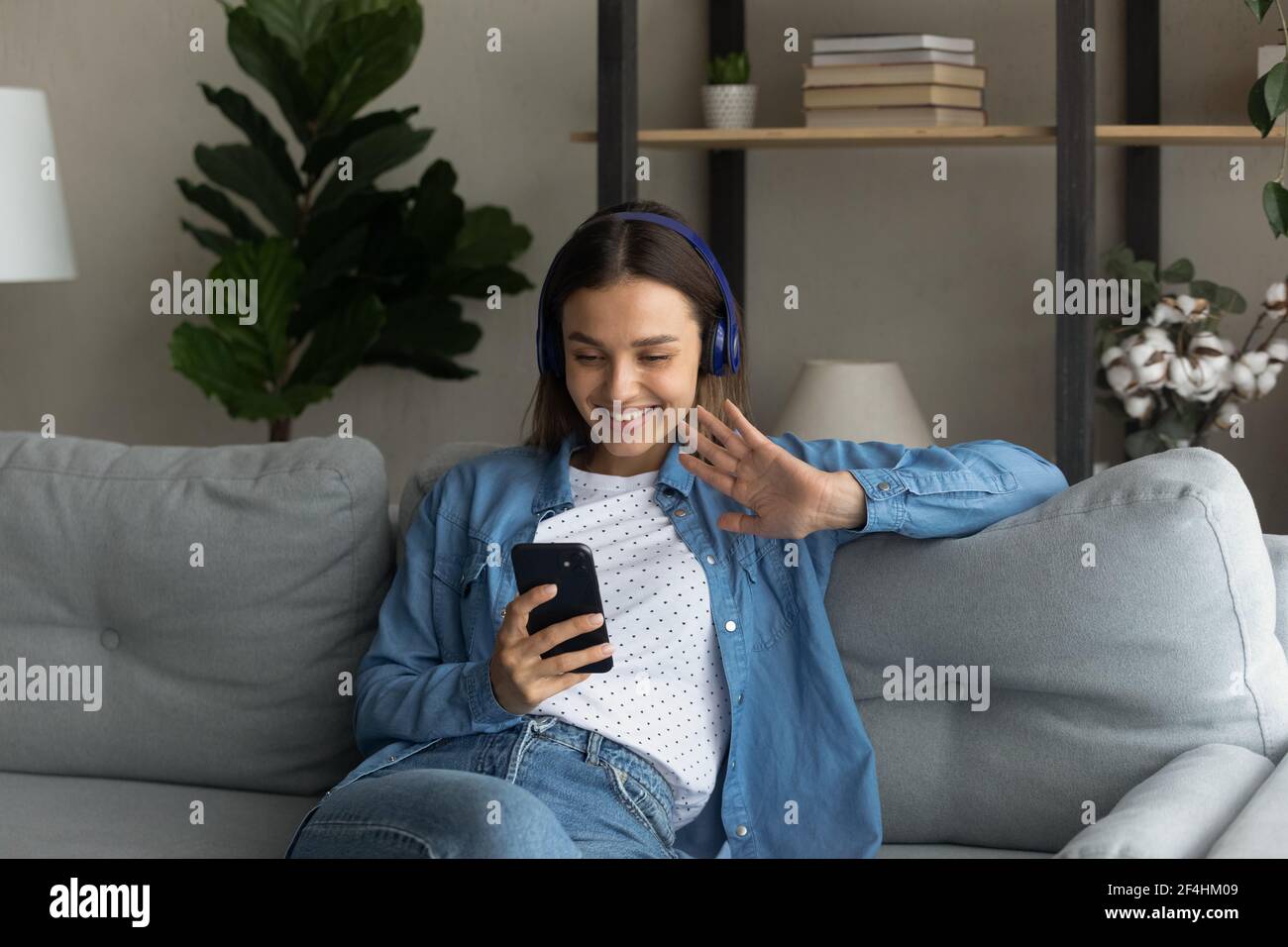 Close up smiling woman wearing headphones waving hand, holding phone Stock Photo - Alamy