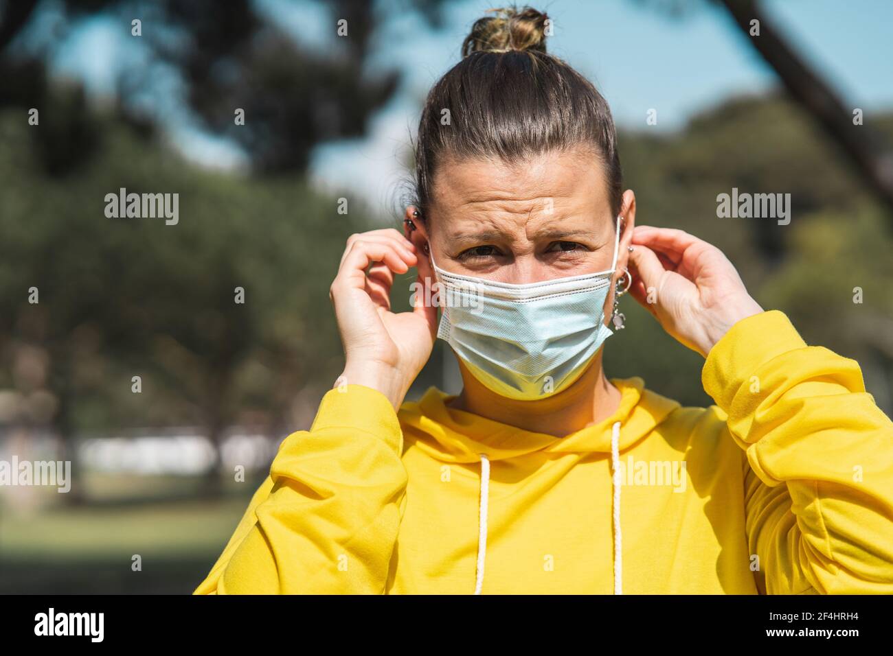A young Spanish girl adjusting her face mask with a frowning face on a ...