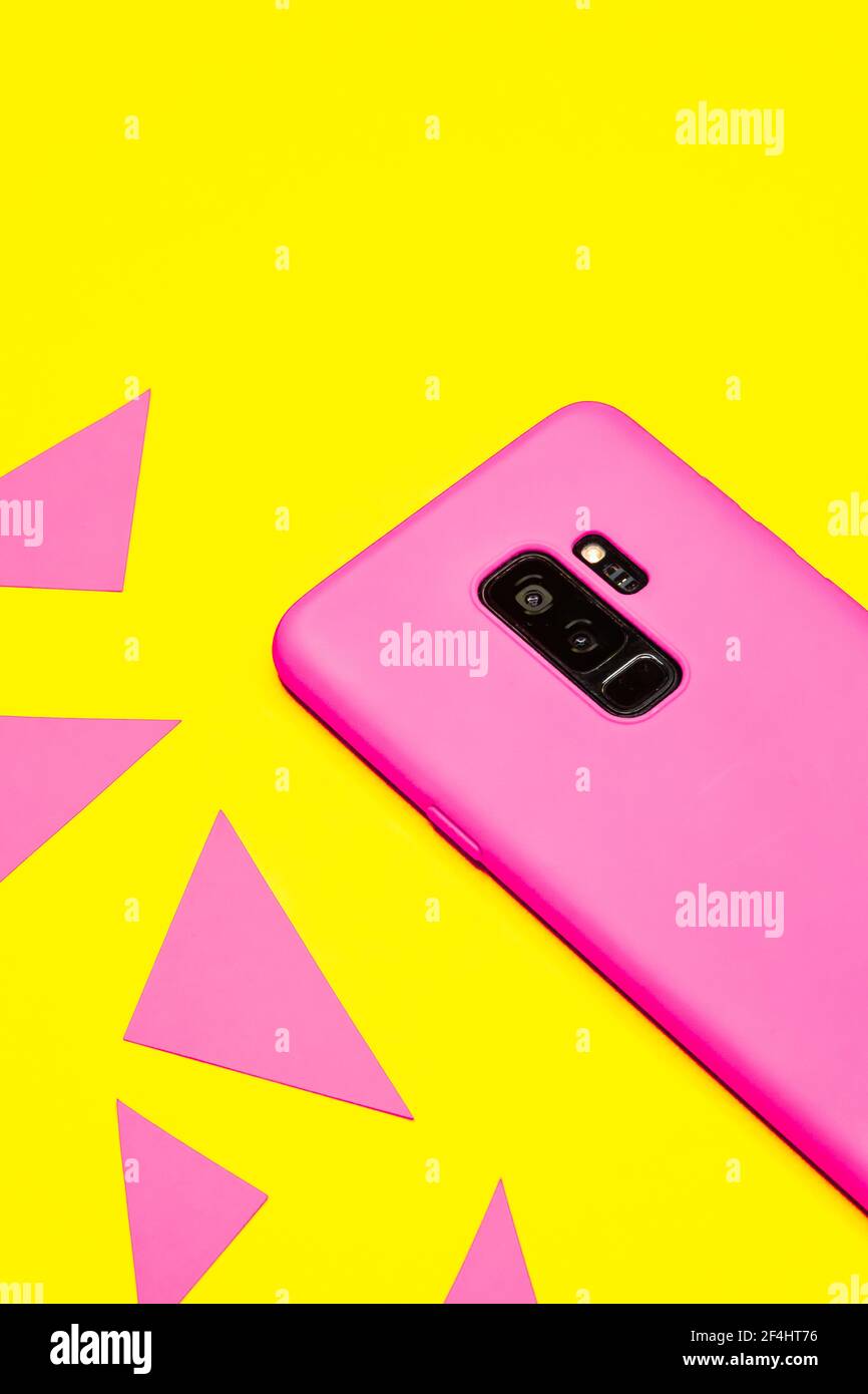 A modern pink mobile phone on a yellow background with pink triangles ...