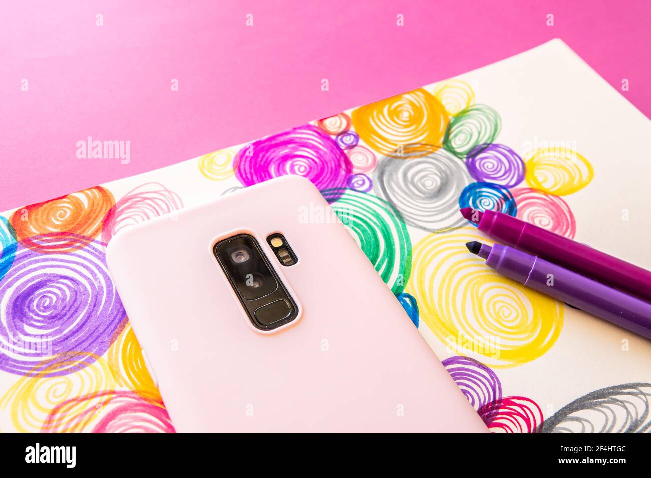 Modern light pink mobile phone on a drawing of colorful spirals next to ...