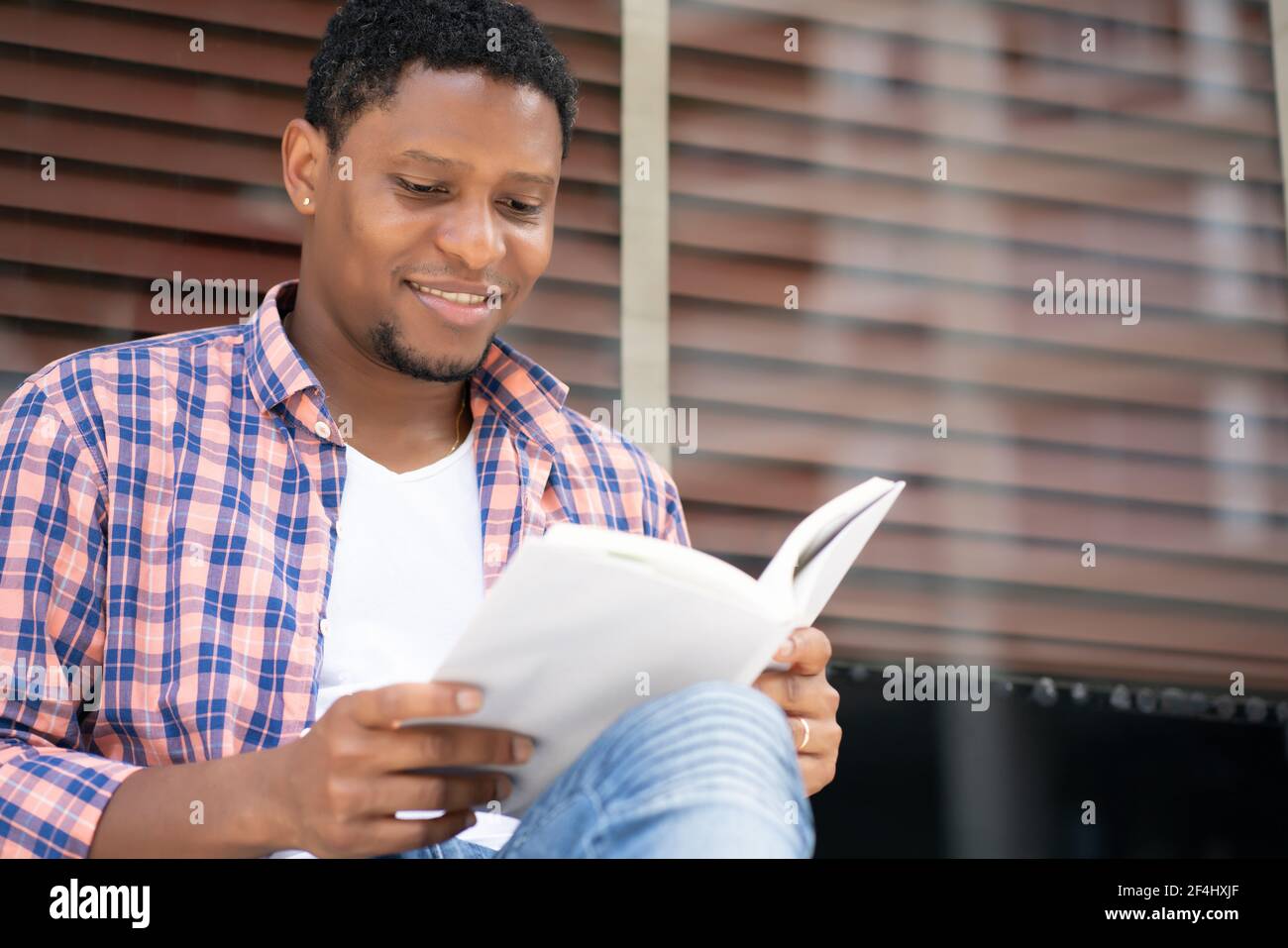 Man reading a book while sitting at a store window Stock Photo - Alamy
