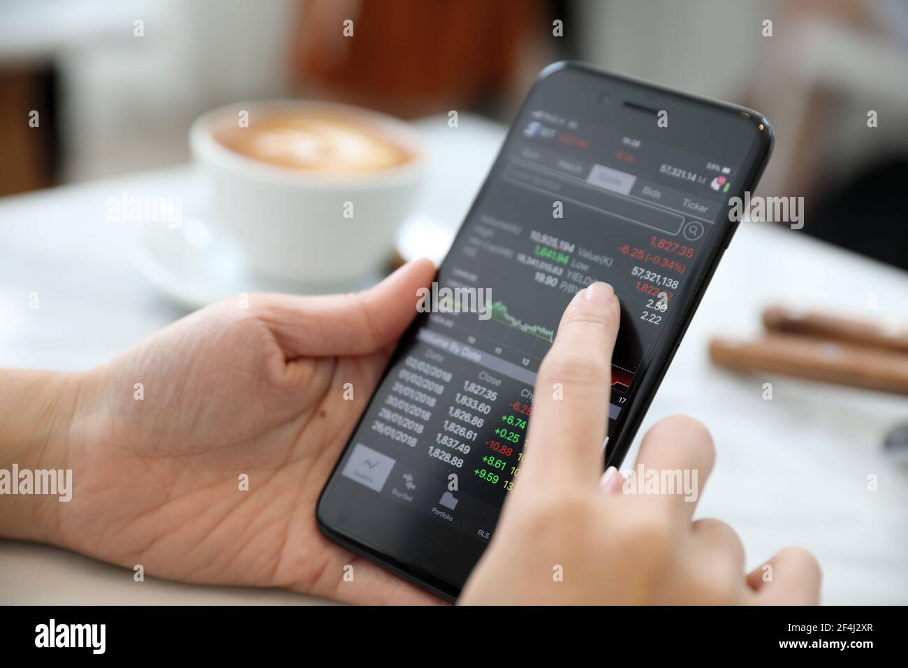 Female hand with smartphone trading stock online in coffee shop ...