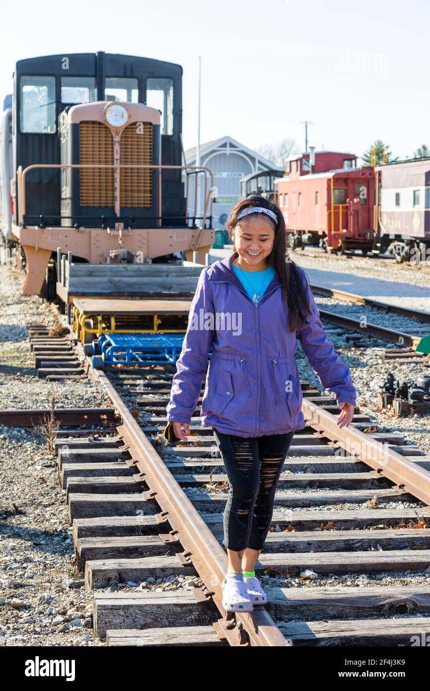 A smiling young woman balances on the rail of a railroad track at the ...
