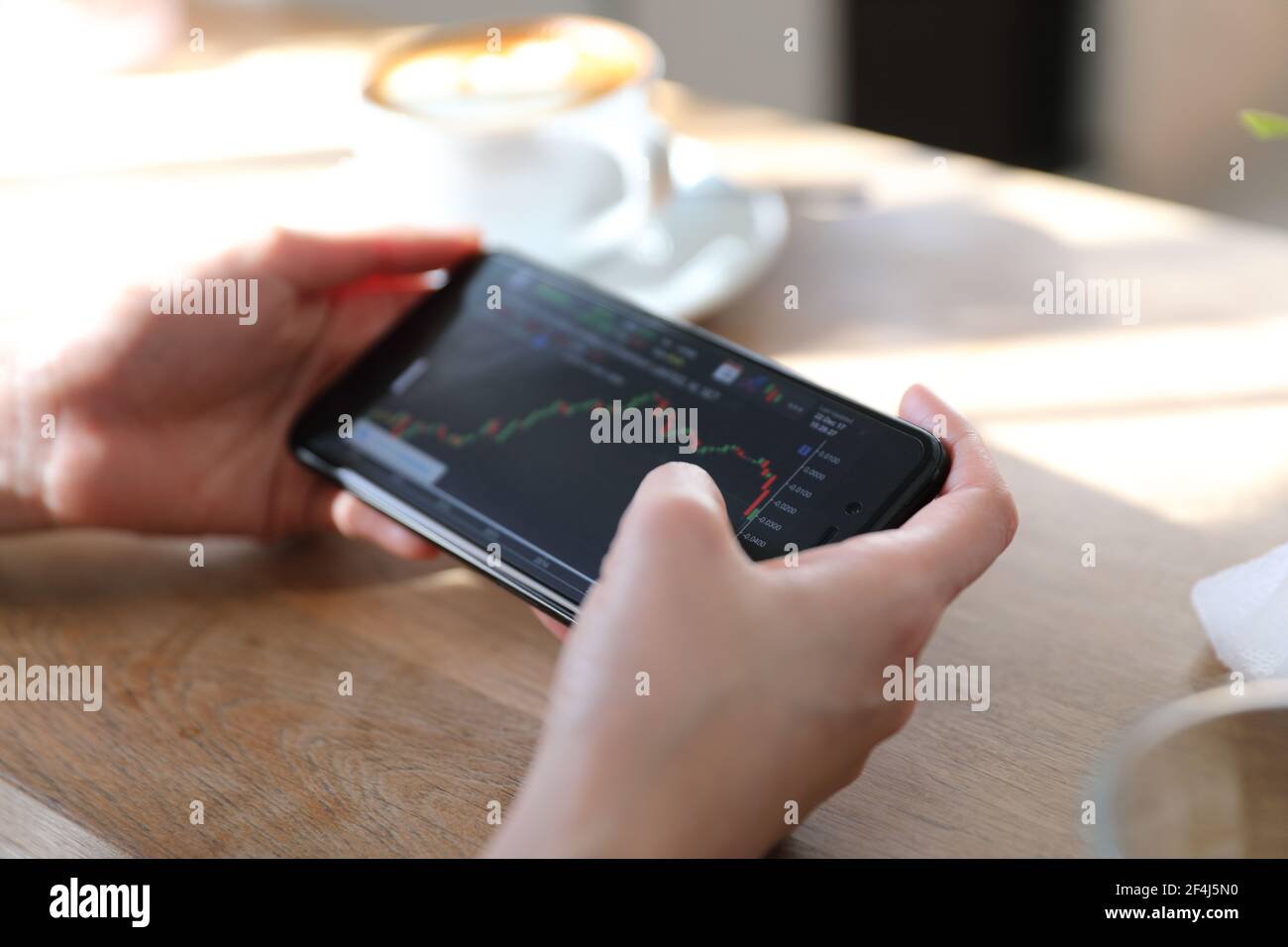 Woman hand trading stock with mobile phone on coffee shop background ...