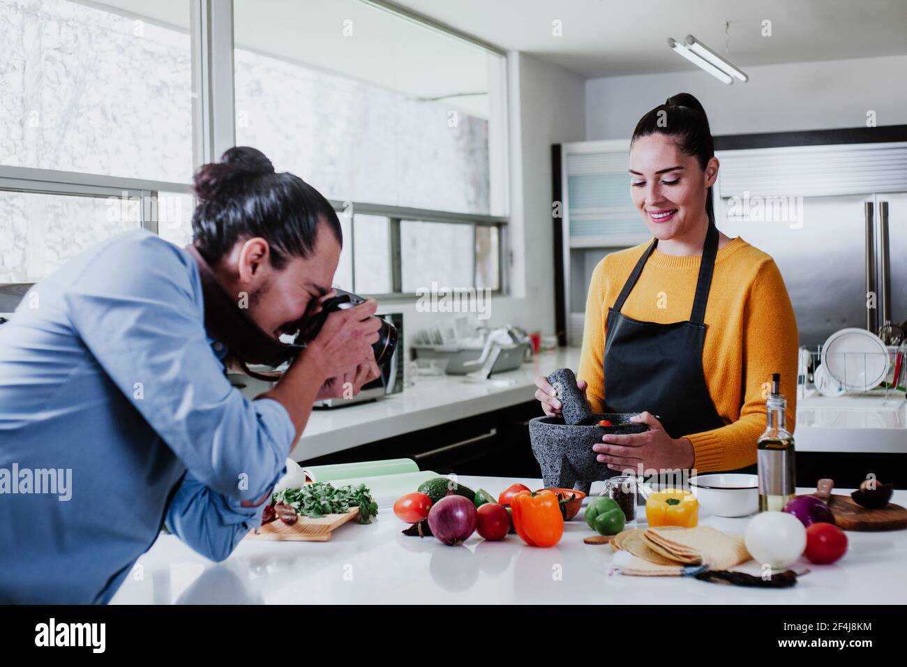 latin couple cooking mexican sauce and food taking photo in the kitchen ...