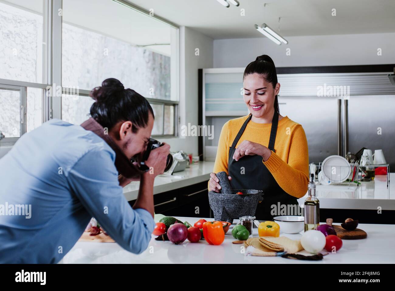 latin couple cooking mexican sauce and food taking photo in the kitchen ...