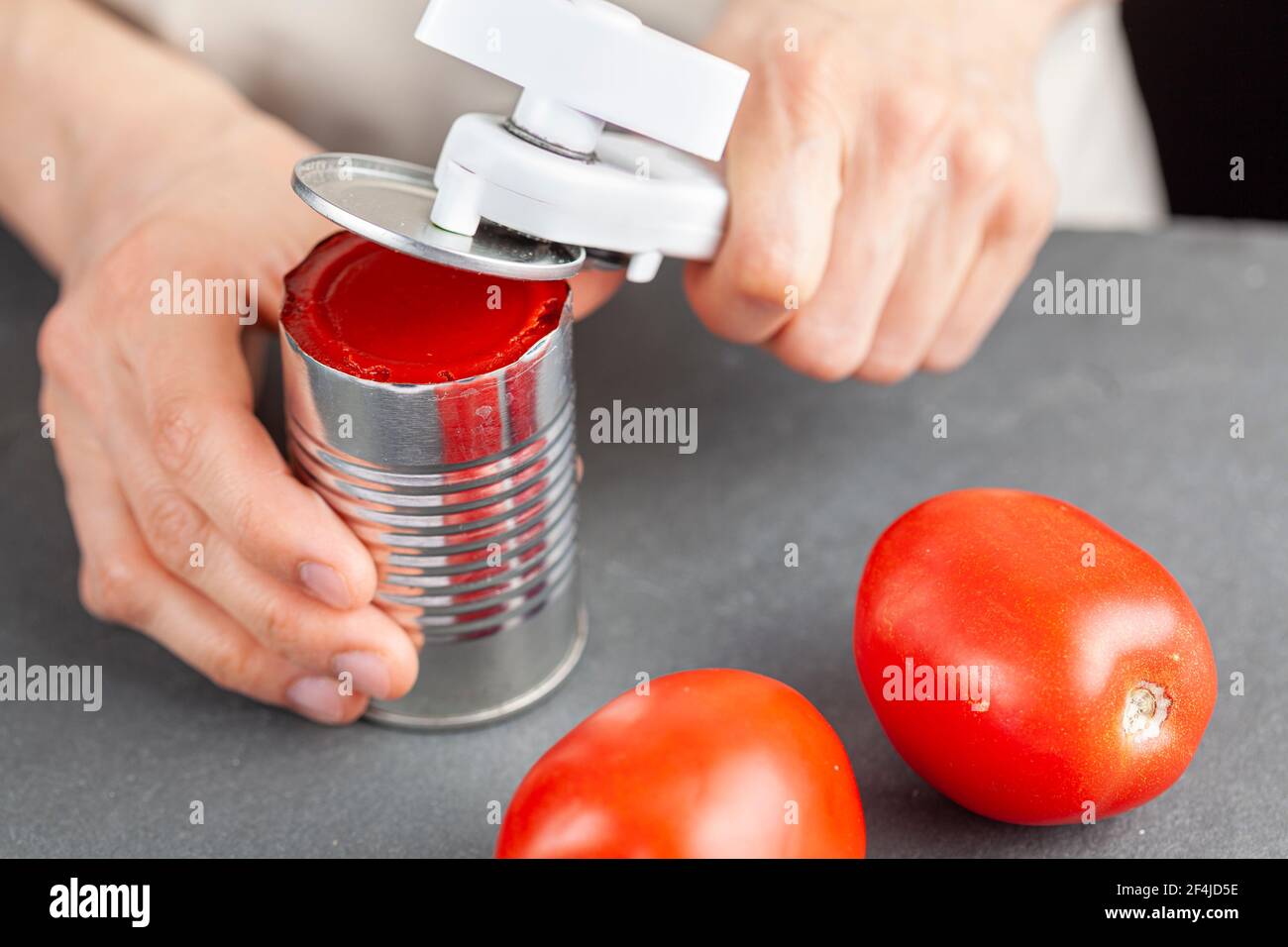 A woman is carefully opening a can of tomato paste on a kitchen counter ...
