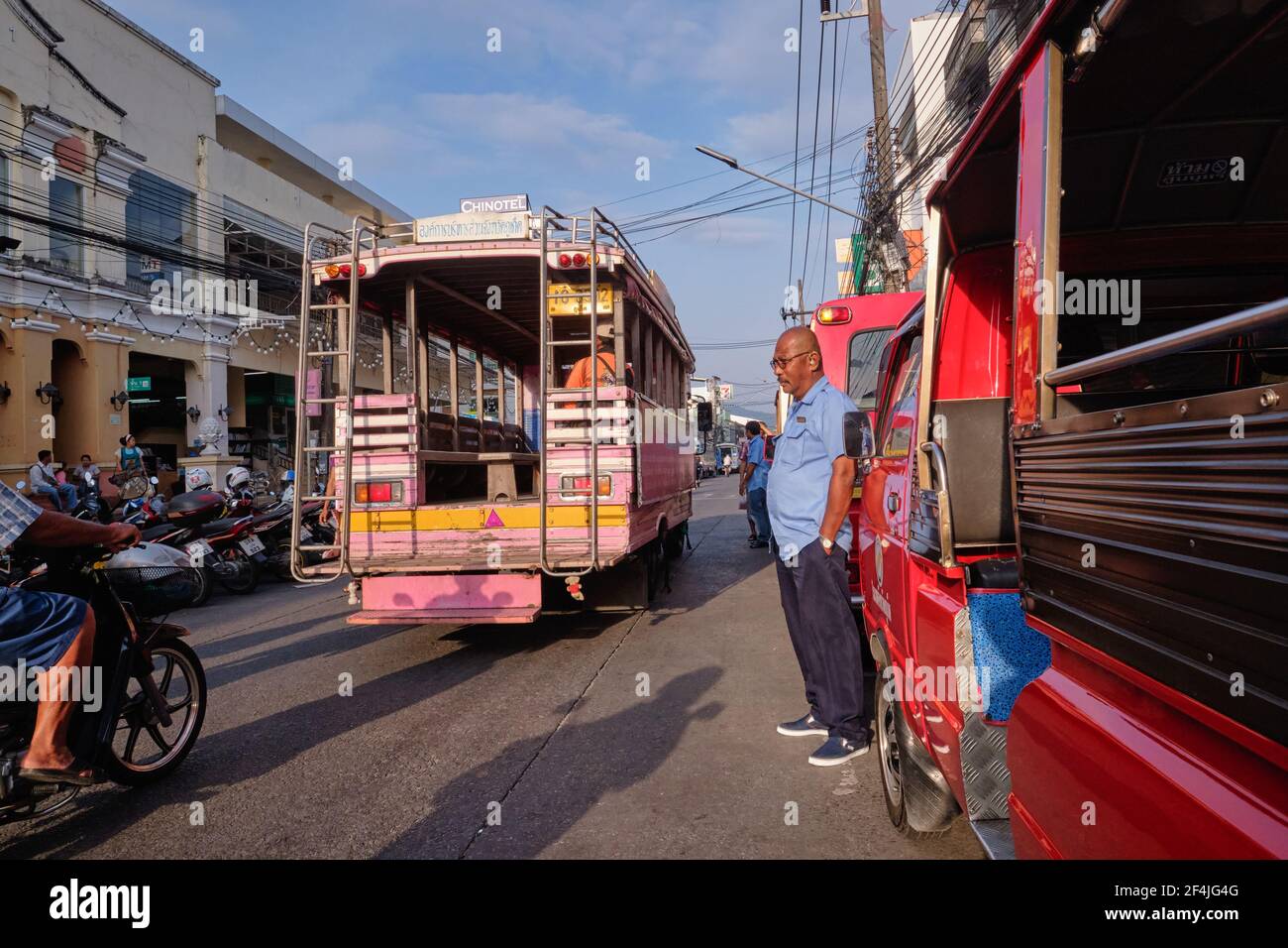 As a local 'songthaew' bus drives past, a tuk-tuk driver stands waiting ...