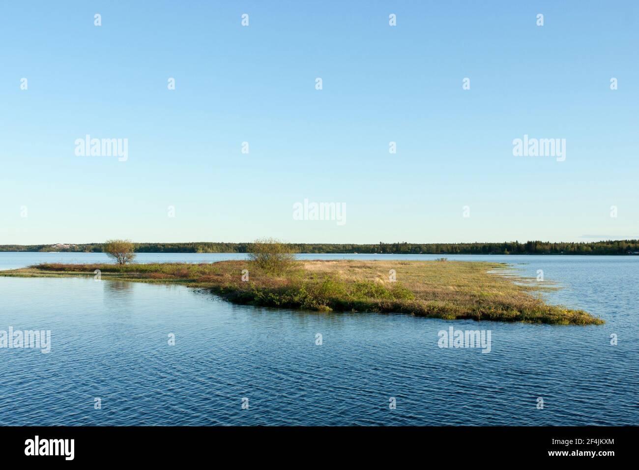 Small grassy island in a river surrounded by water. Blue sky and ...