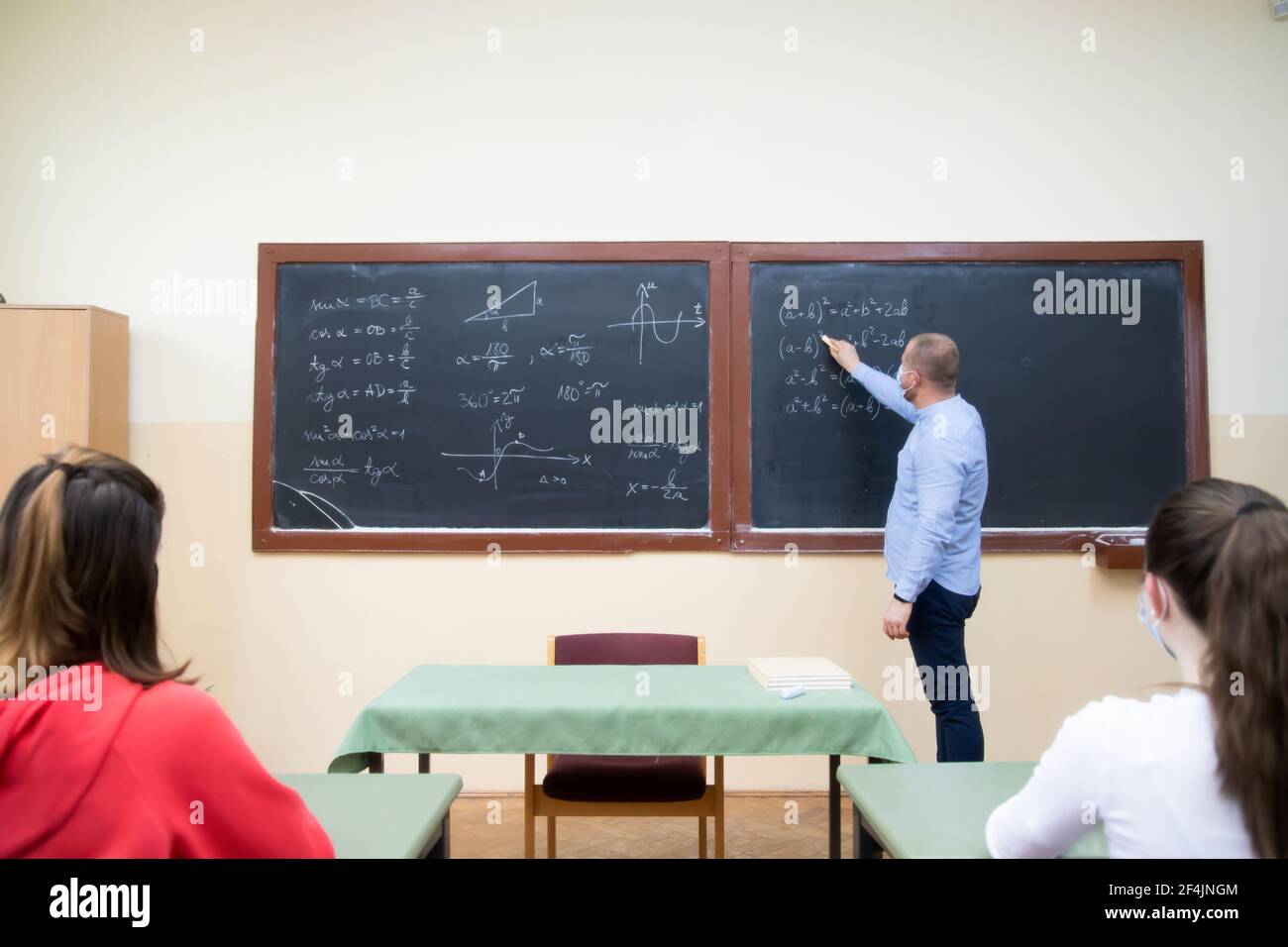 Teacher and his students wearing protective face mask in the classroom ...