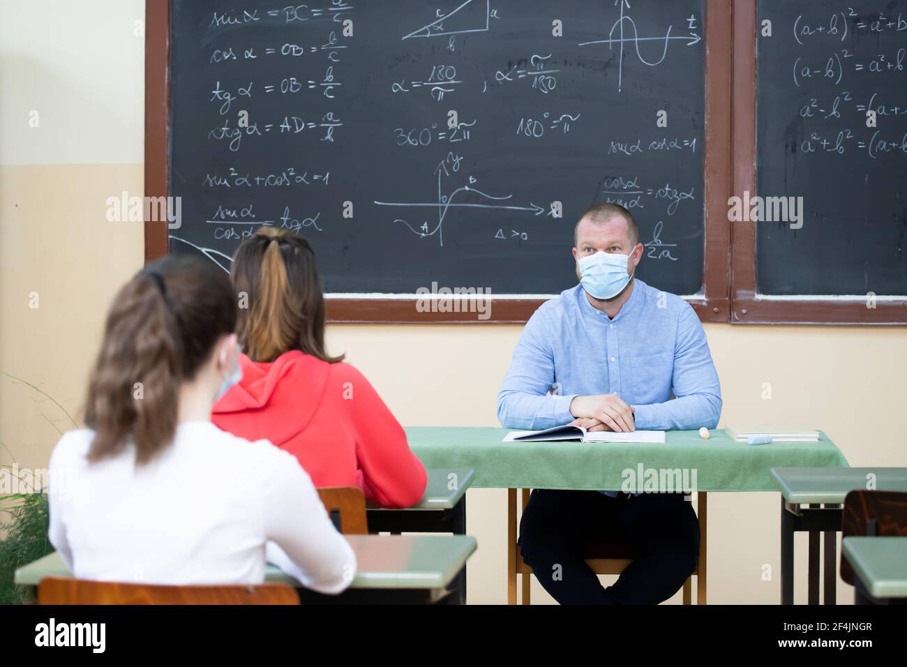 Teacher and his students wearing protective face mask in the classroom ...