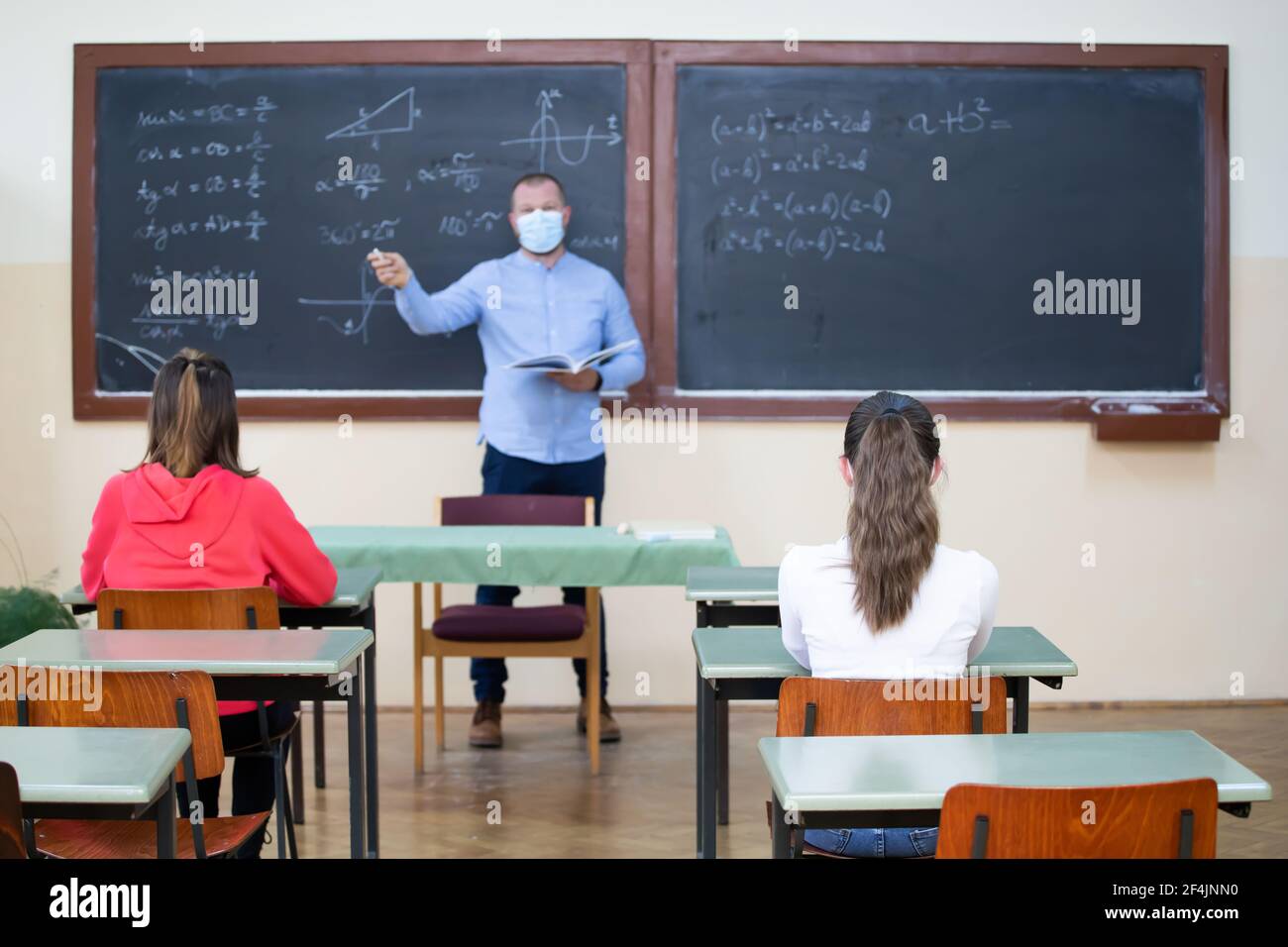 Teacher and his students wearing protective face mask in the classroom ...
