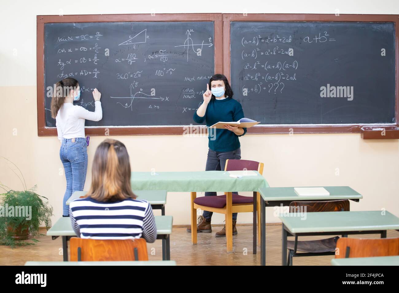 Teacher and her students wearing protective face mask in the classroom ...