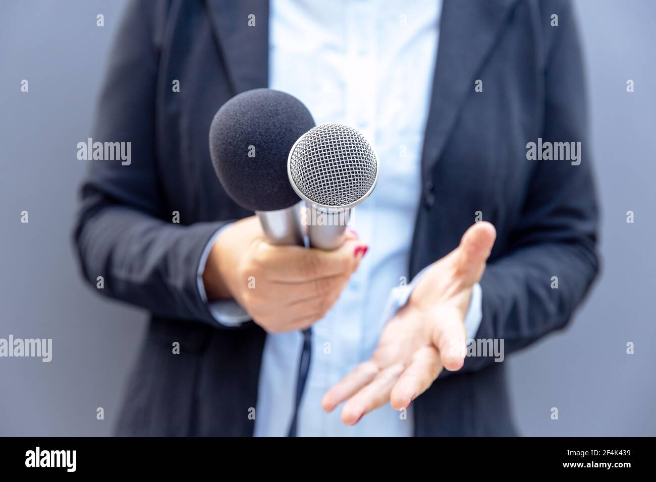 Female TV reporter or journalist holding microphone and making media interview. Broadcast ...