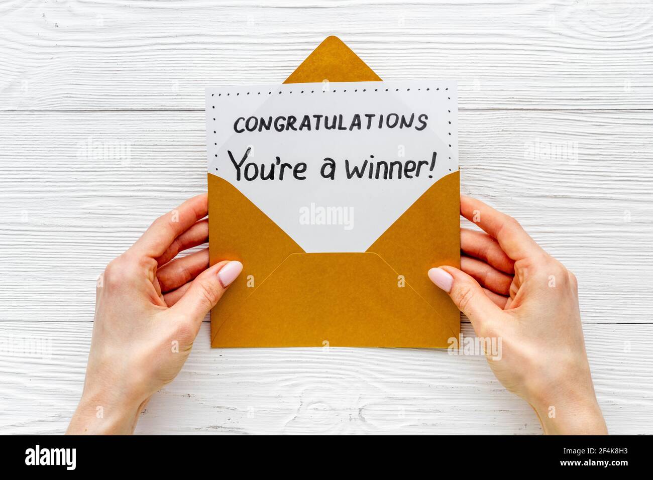 Hands holding award congratulation card in golden envelope. Text You're ...