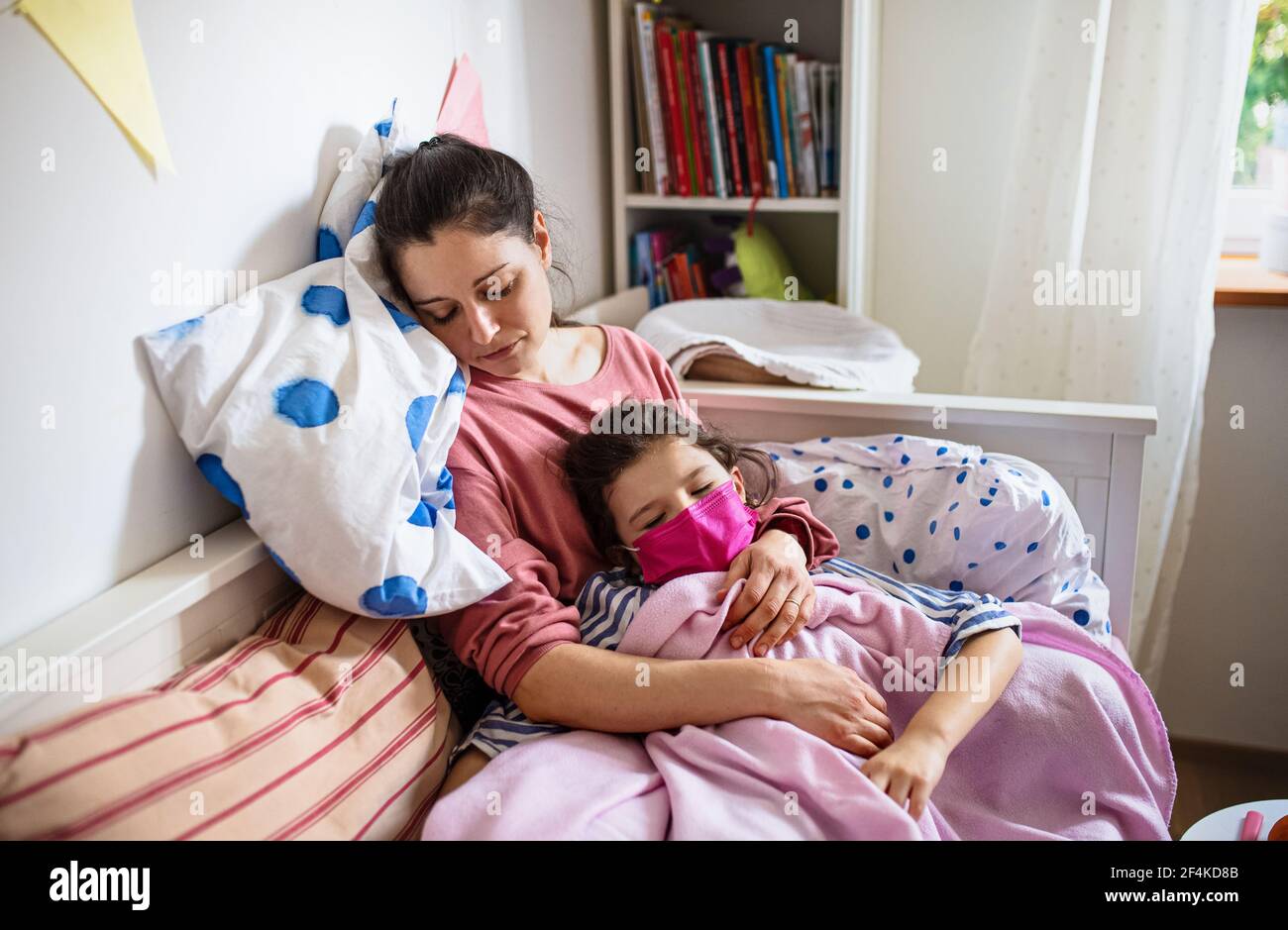 Tired mother looking after sick small daughter in bed at home ...