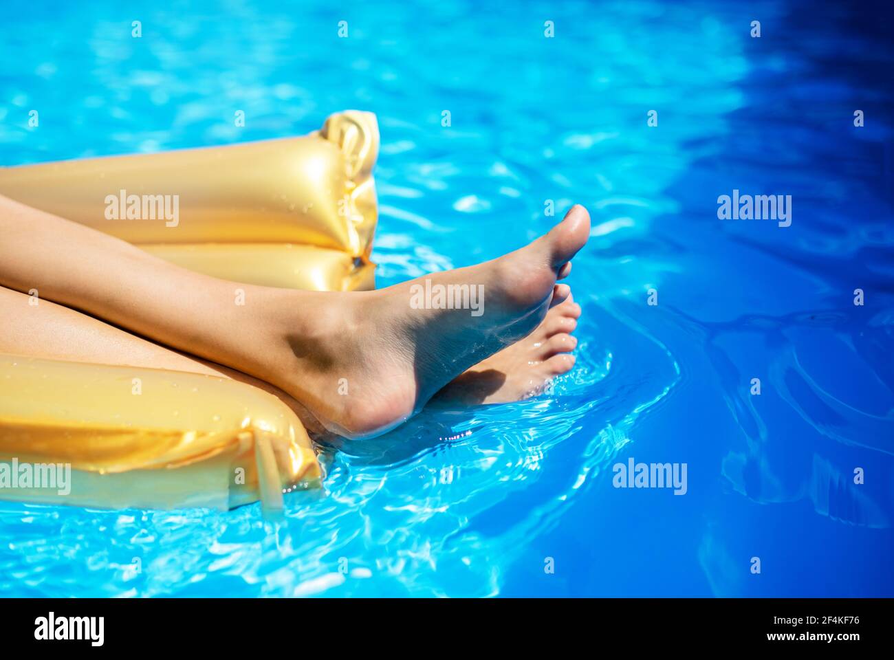 Close up of females feet on floating bed in swimming pool outdoors ...