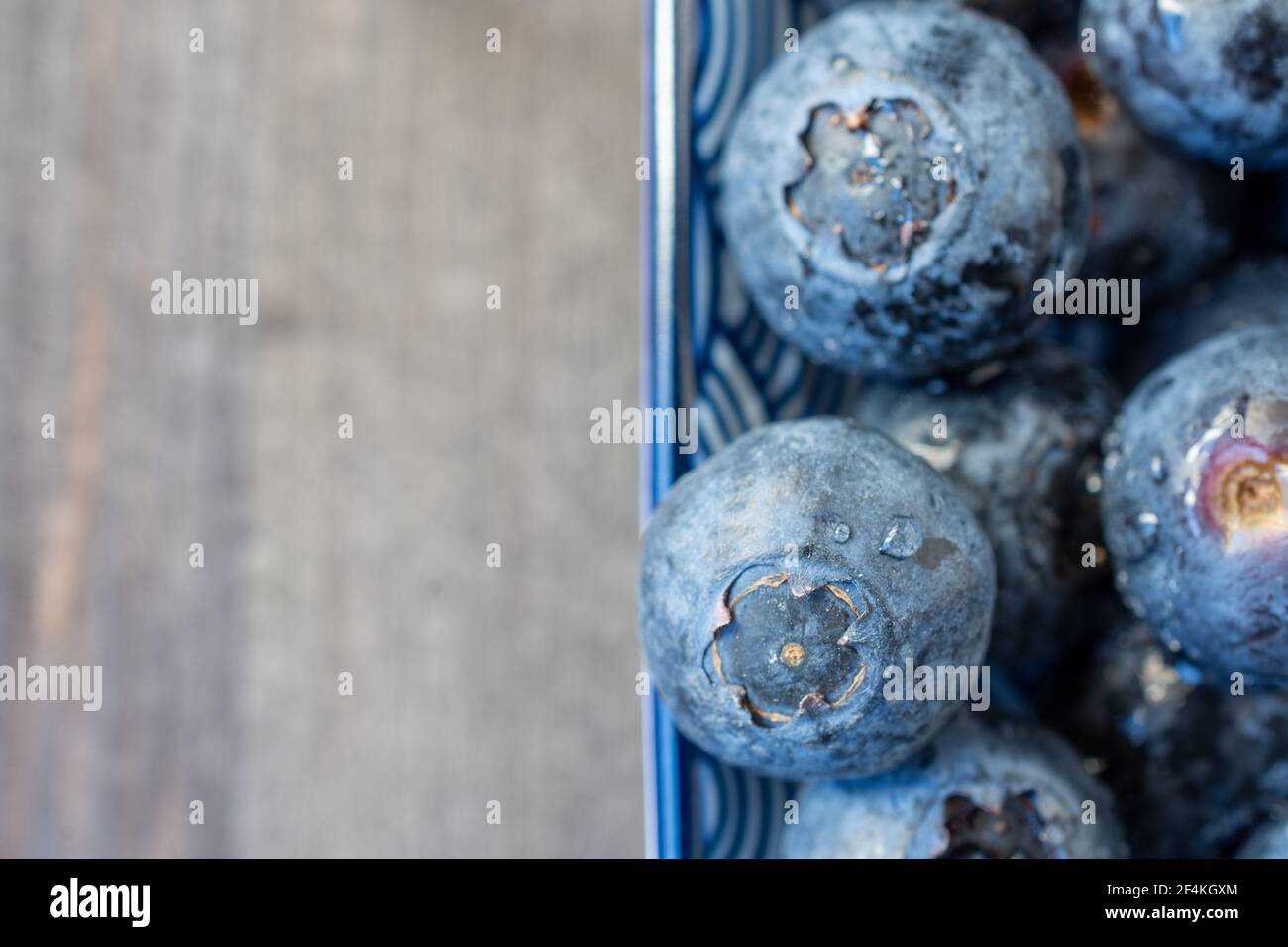 Close-up of a group of wet dark blueberries, in bowl, on wooden table ...