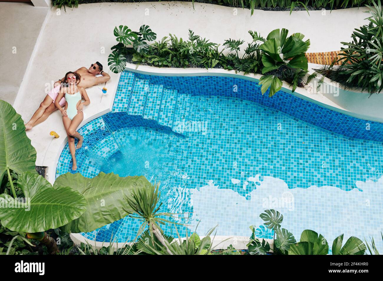 Happy beautiful couple sunbathing by swimming pool of spa hotel with ...