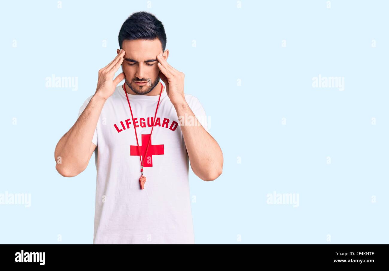 Young handsome man wearing lifeguard uniform with hand on head for pain ...