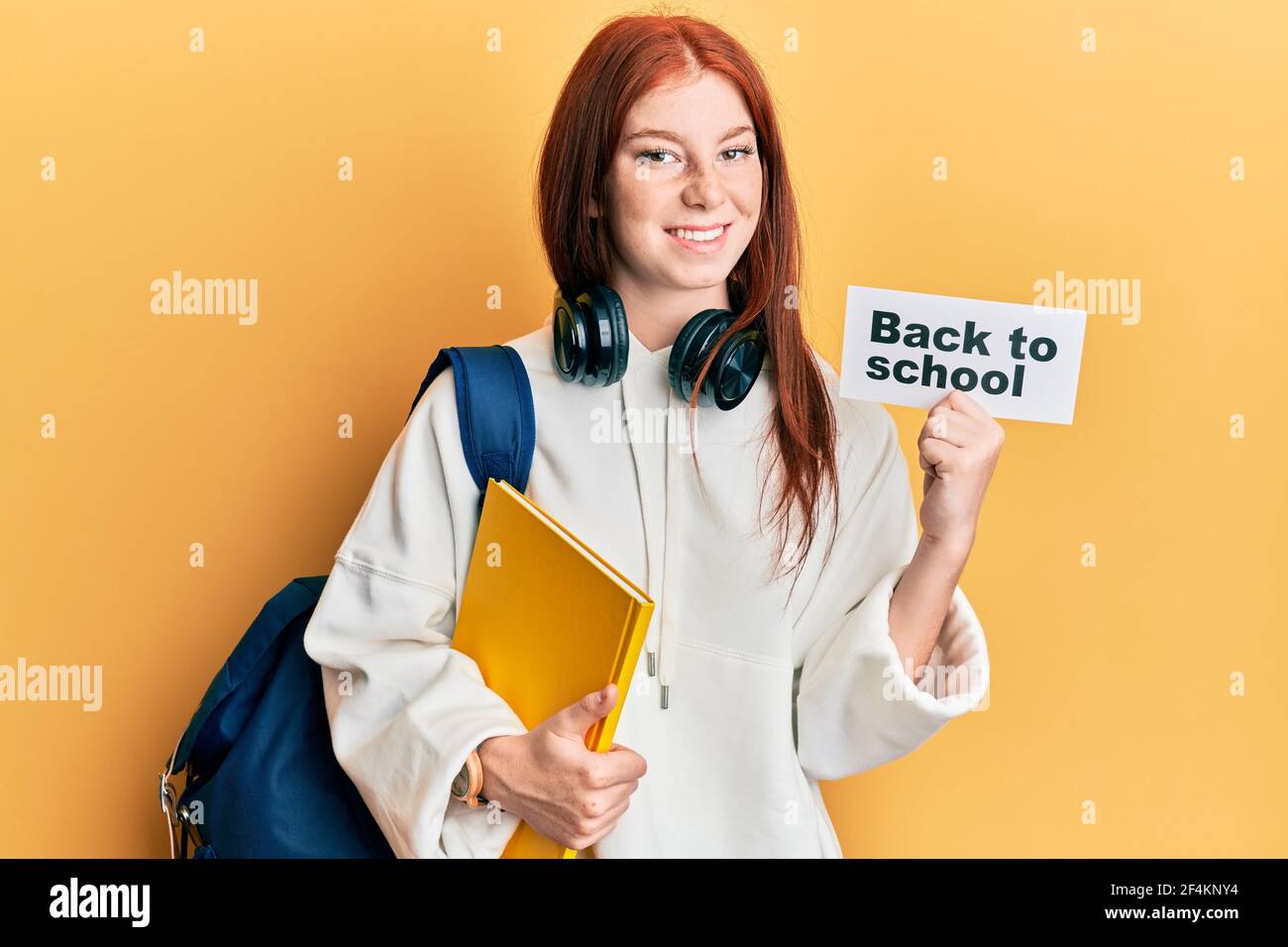 Young red head girl wearing backpack holding back to school banner ...