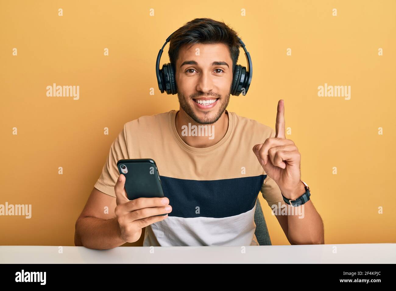 Young handsome man using smartphone wearing headphones smiling with an ...