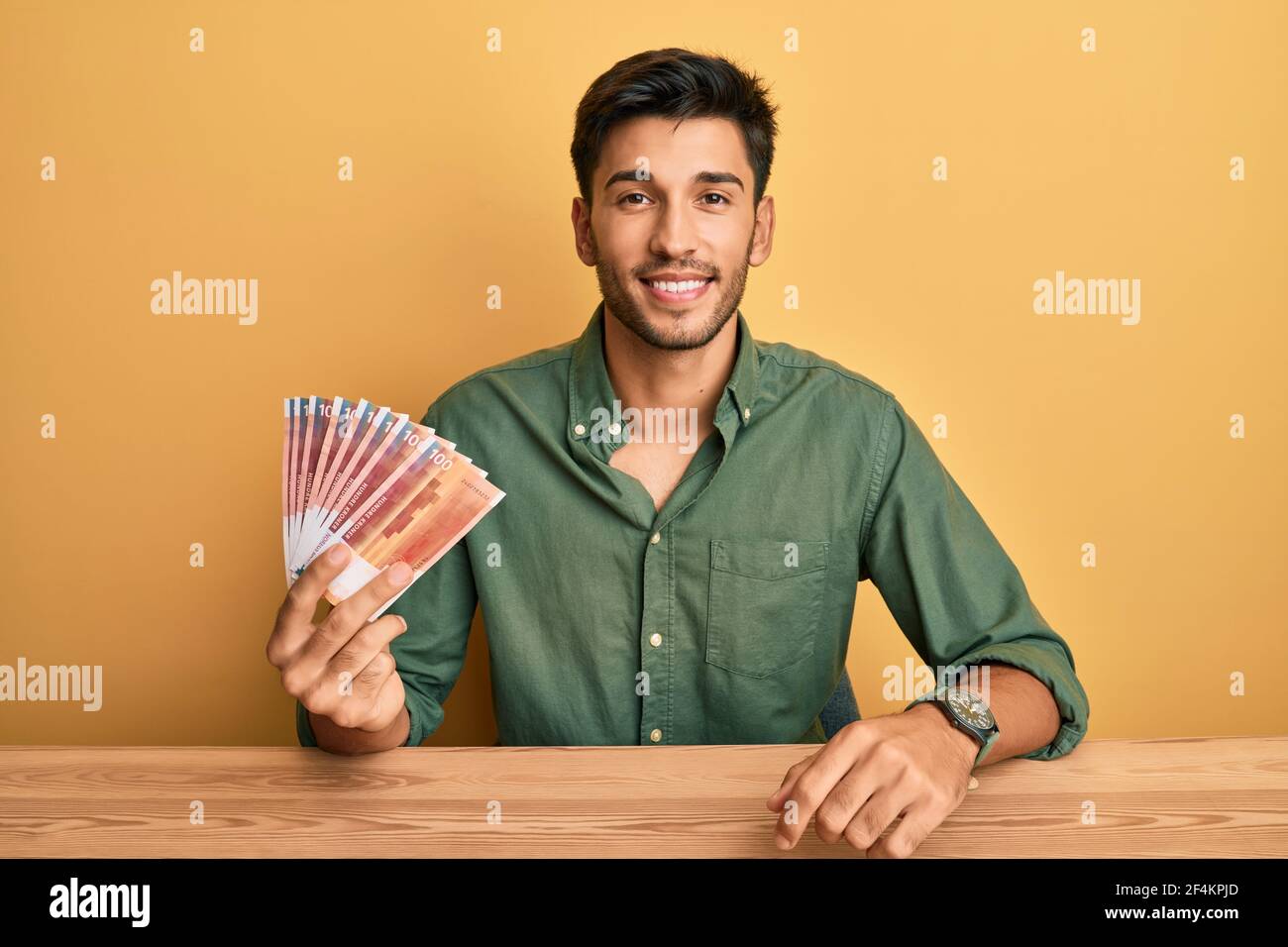 Young handsome man holding norwegian krone banknotes looking positive ...
