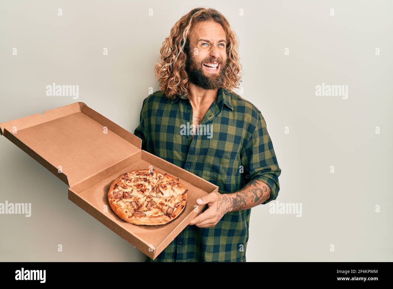 Handsome man with beard and long hair holding italian pizza angry and ...