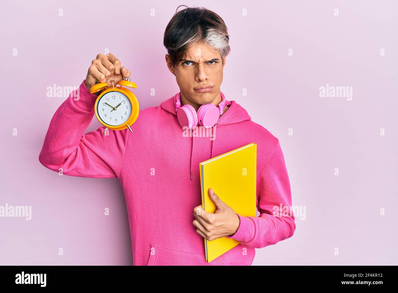 Young hispanic man holding book and alarm clock skeptic and nervous ...