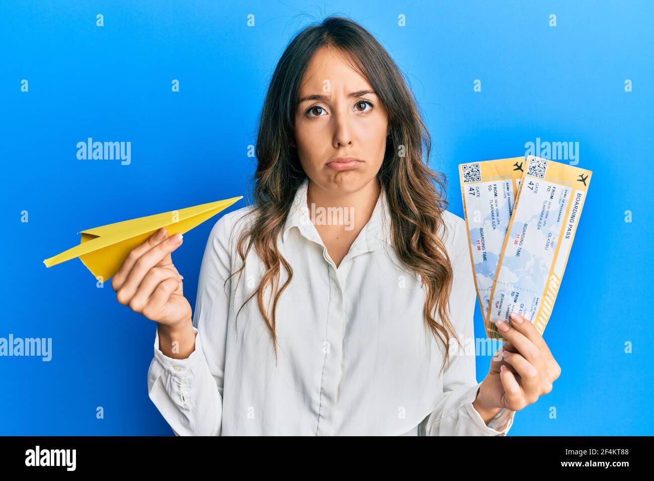 Young brunette woman holding paper airplane and boarding pass depressed ...