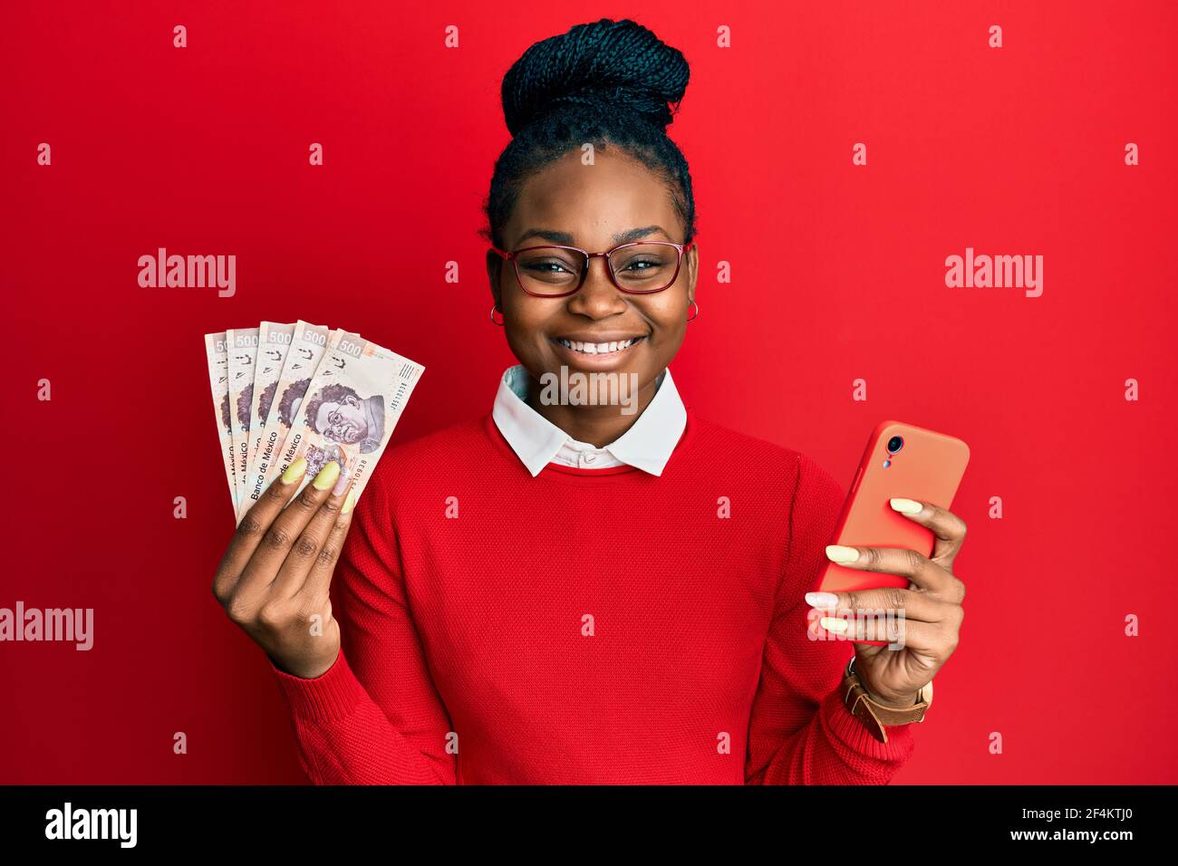 Young african american woman using smartphone holding mexican peso ...