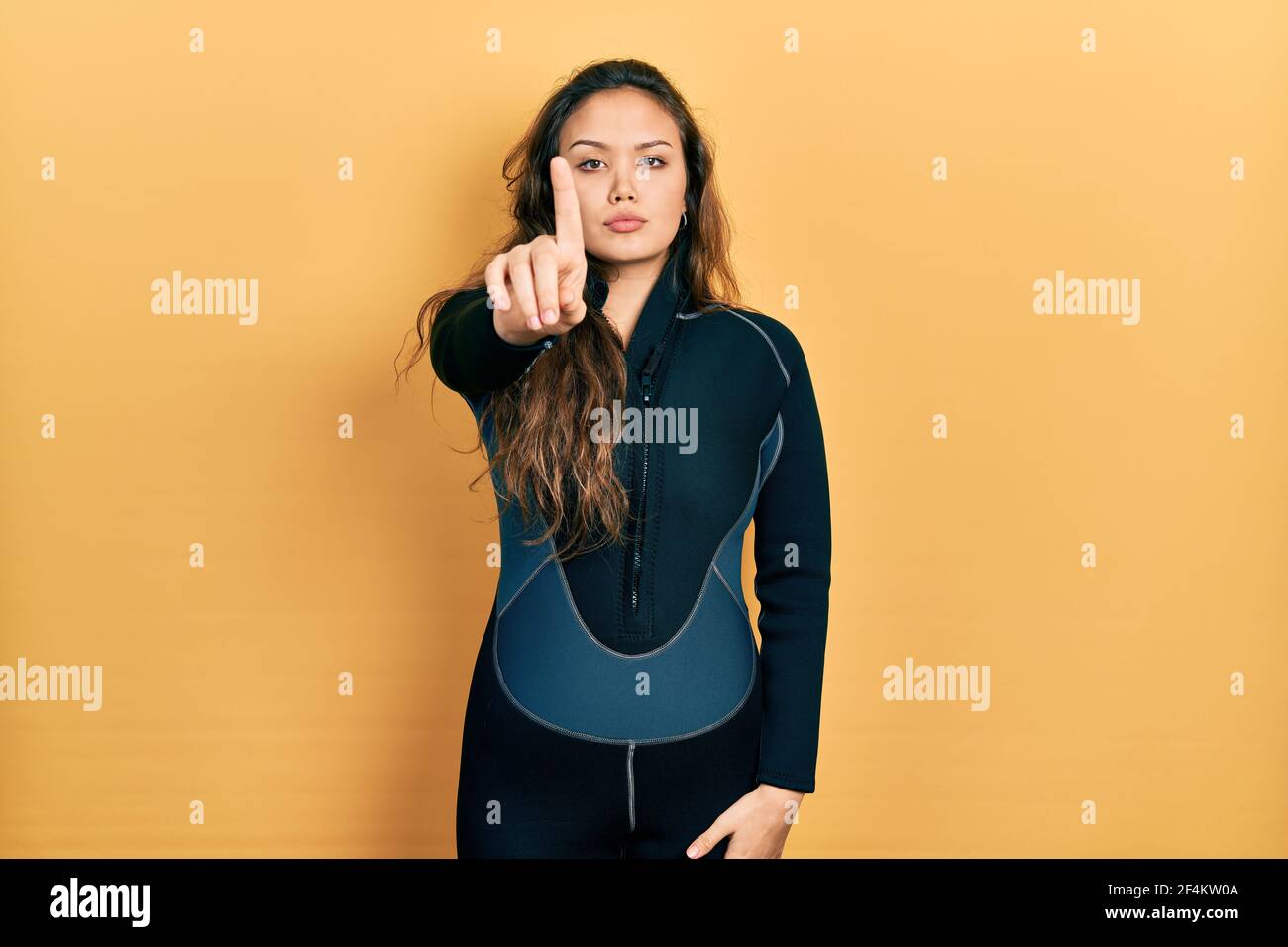 Young hispanic girl wearing diver neoprene uniform pointing with finger ...