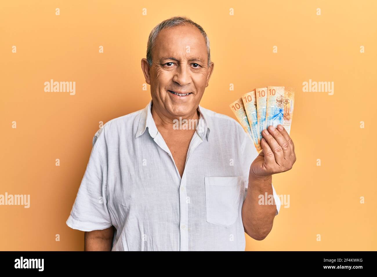 Handsome mature man holding swiss franc banknotes looking positive and ...