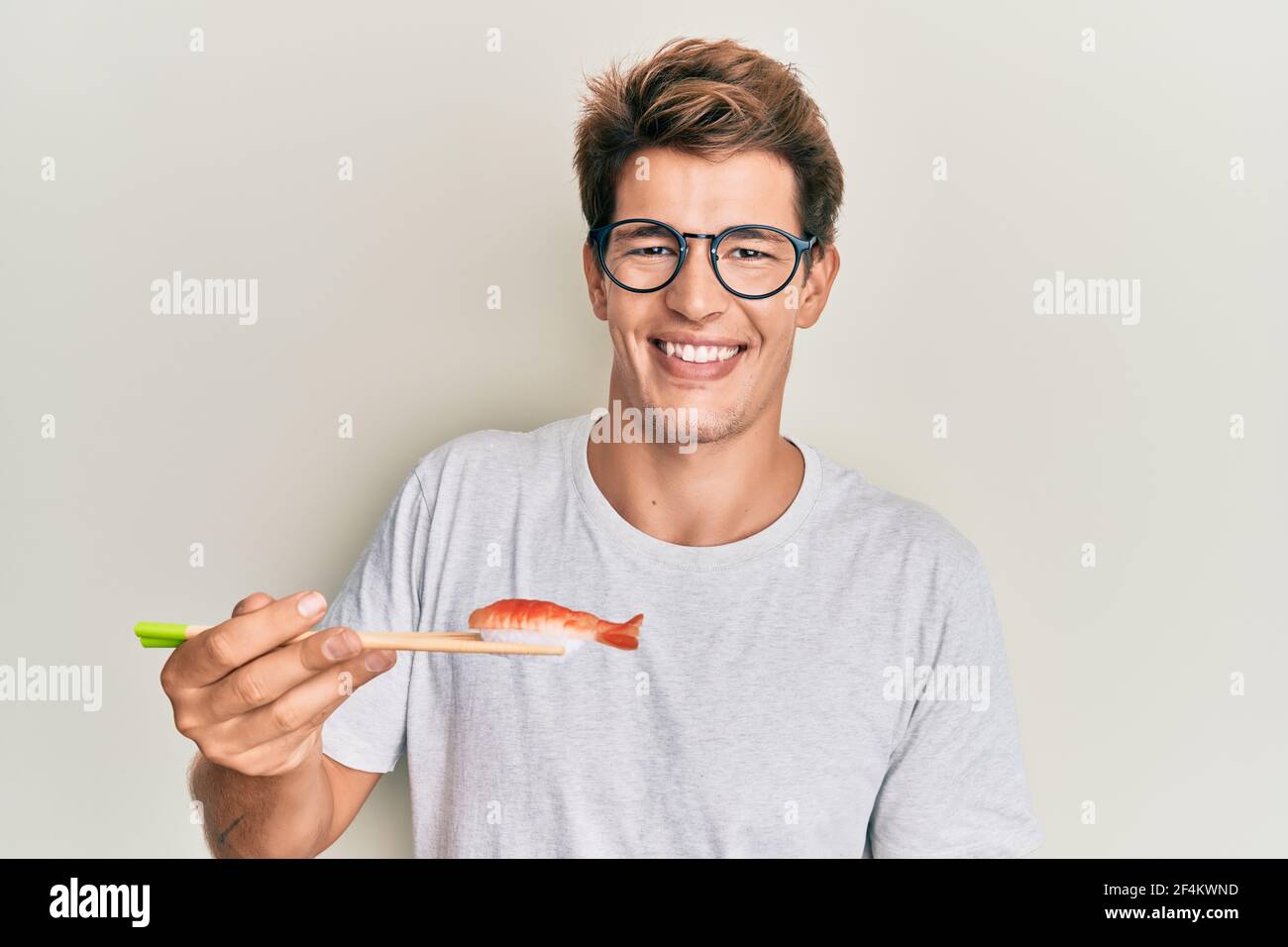 Handsome caucasian man eating prawn sushi using chopsticks looking ...