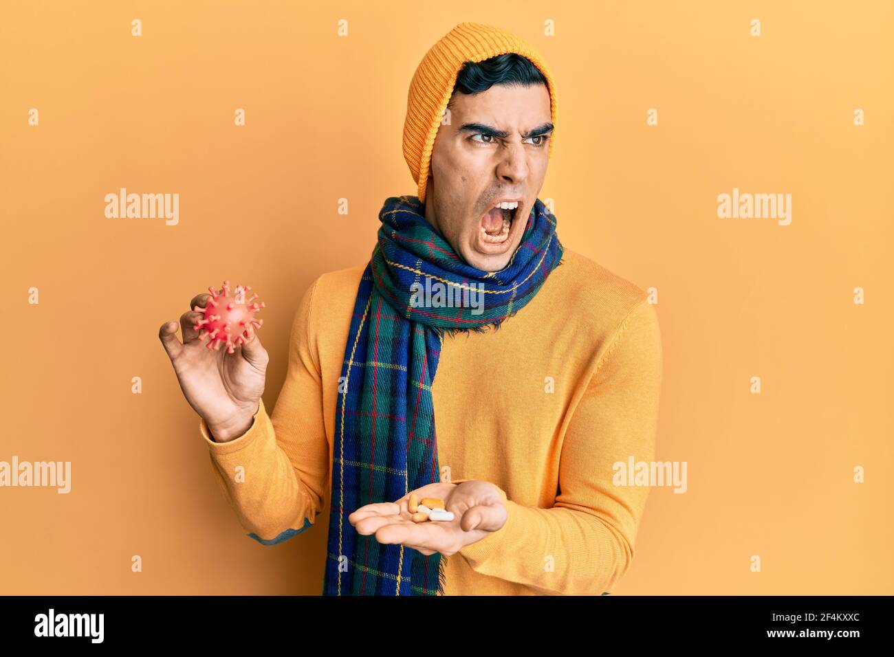 Handsome hispanic man holding virus toy and pills angry and mad ...