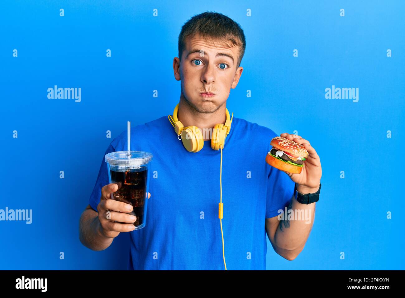 Young caucasian man eating a tasty classic burger and soda puffing ...
