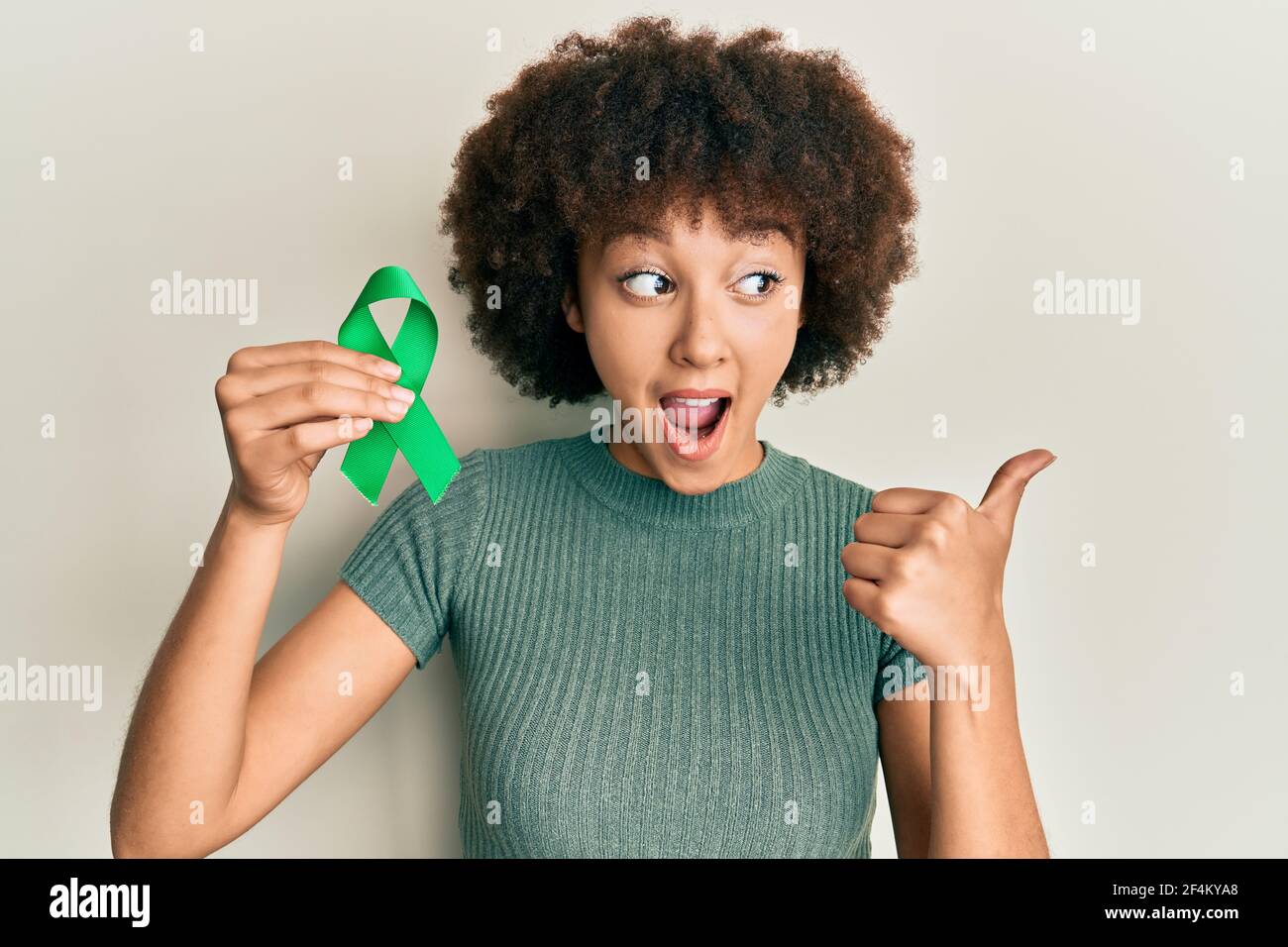 Young hispanic girl holding support green ribbon pointing thumb up to ...