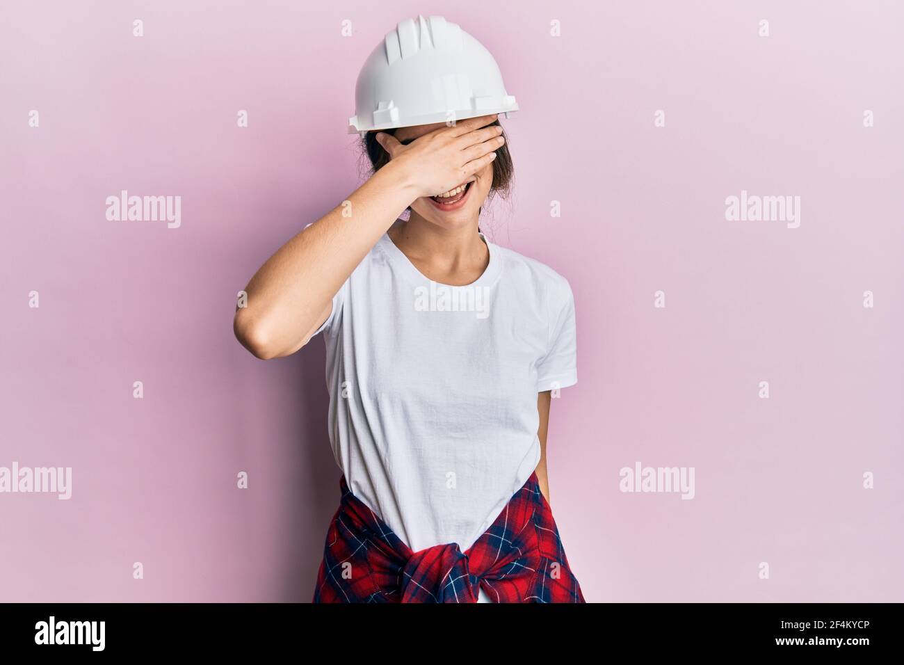Young caucasian woman wearing hardhat smiling and laughing with hand on ...