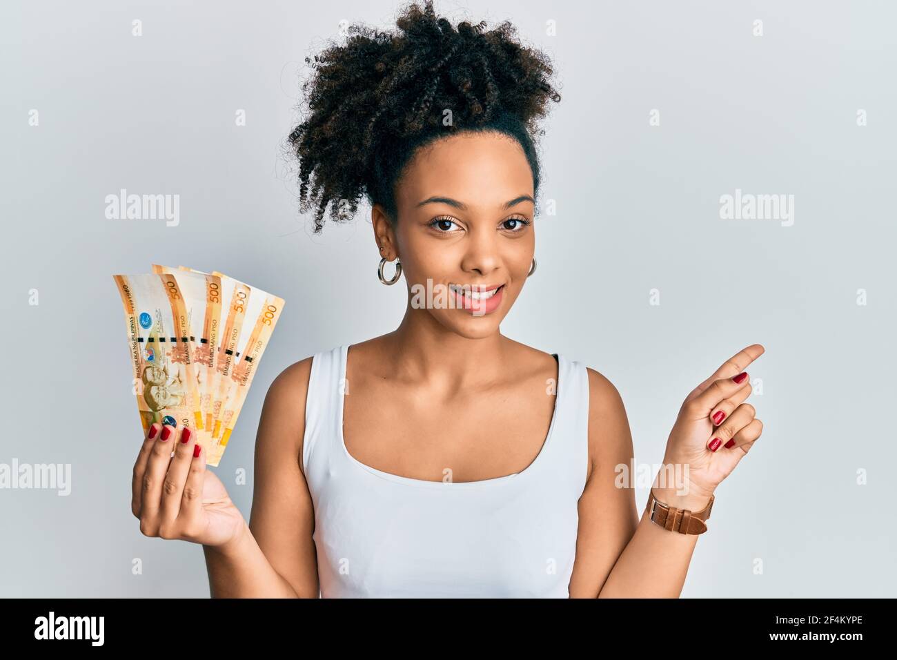 Young african american girl holding philippine peso banknotes smiling ...
