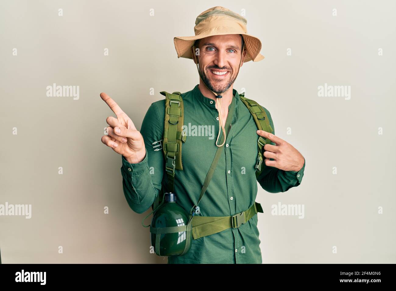 Handsome man with beard wearing explorer hat and backpack cheerful with ...